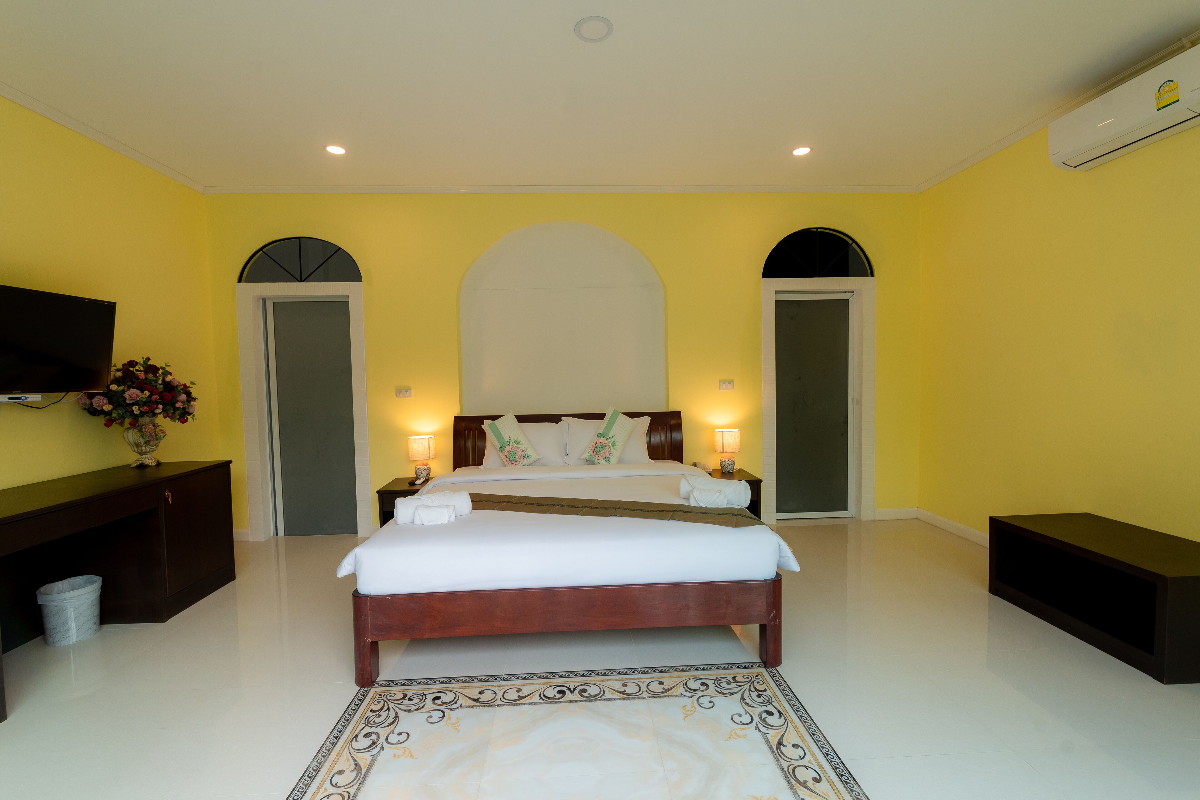 Quarto de hotel com uma cama grande, duas mesinhas de cabeceira, uma televisão e um vaso decorativo.