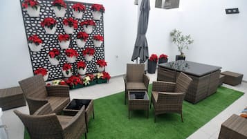 Área de pátio com móveis de vime, uma mesa e parede decorativa com plantas em vasos.