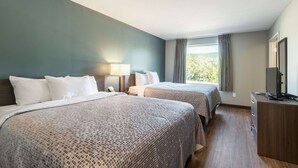 Quarto de hotel com duas camas, uma escrivaninha, uma televisão e uma janela com cortinas.