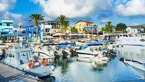 Uma marina com barcos atracados, um calçadão à beira-mar e edifícios com varandas com vista para a água.