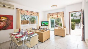 Uma sala de estar moderna com uma mesa de jantar de vidro, dois sofás, uma televisão e um quadro na parede.