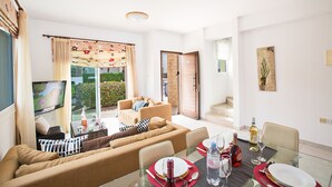 Uma sala de estar moderna com um sofá, uma mesa de jantar posta para dois e uma televisão à esquerda.