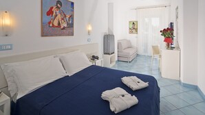 Quarto de hotel com cama, sofá, escrivaninha com um vaso de flores e obras de arte nas paredes.