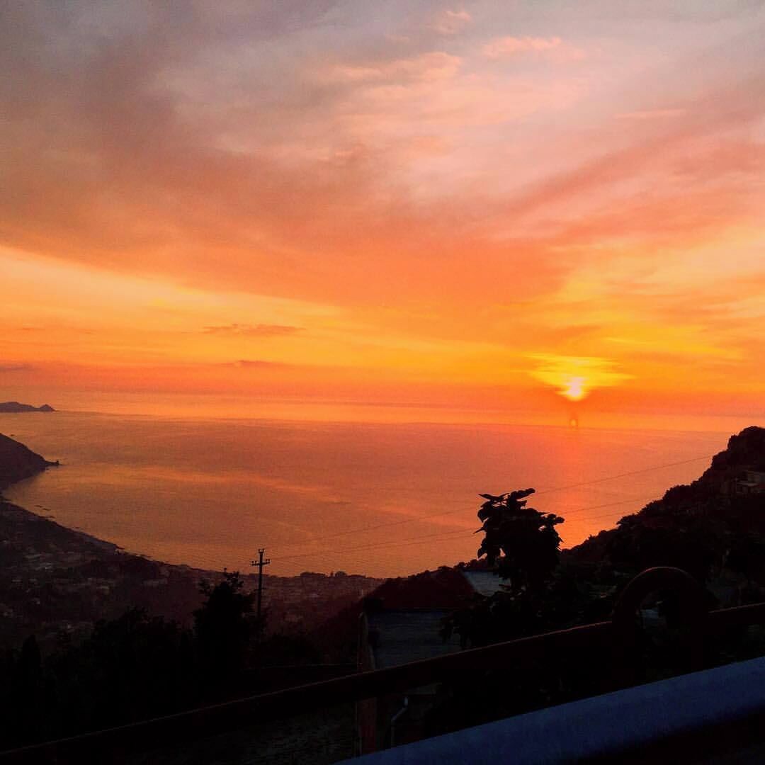 Um pôr do sol sobre a paisagem costeira, com uma estrada em primeiro plano.