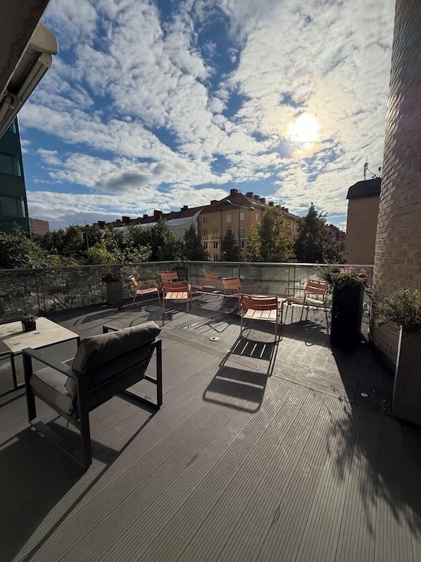Terraço no telhado com mobiliário externo, vista para edifícios e céu parcialmente nublado.