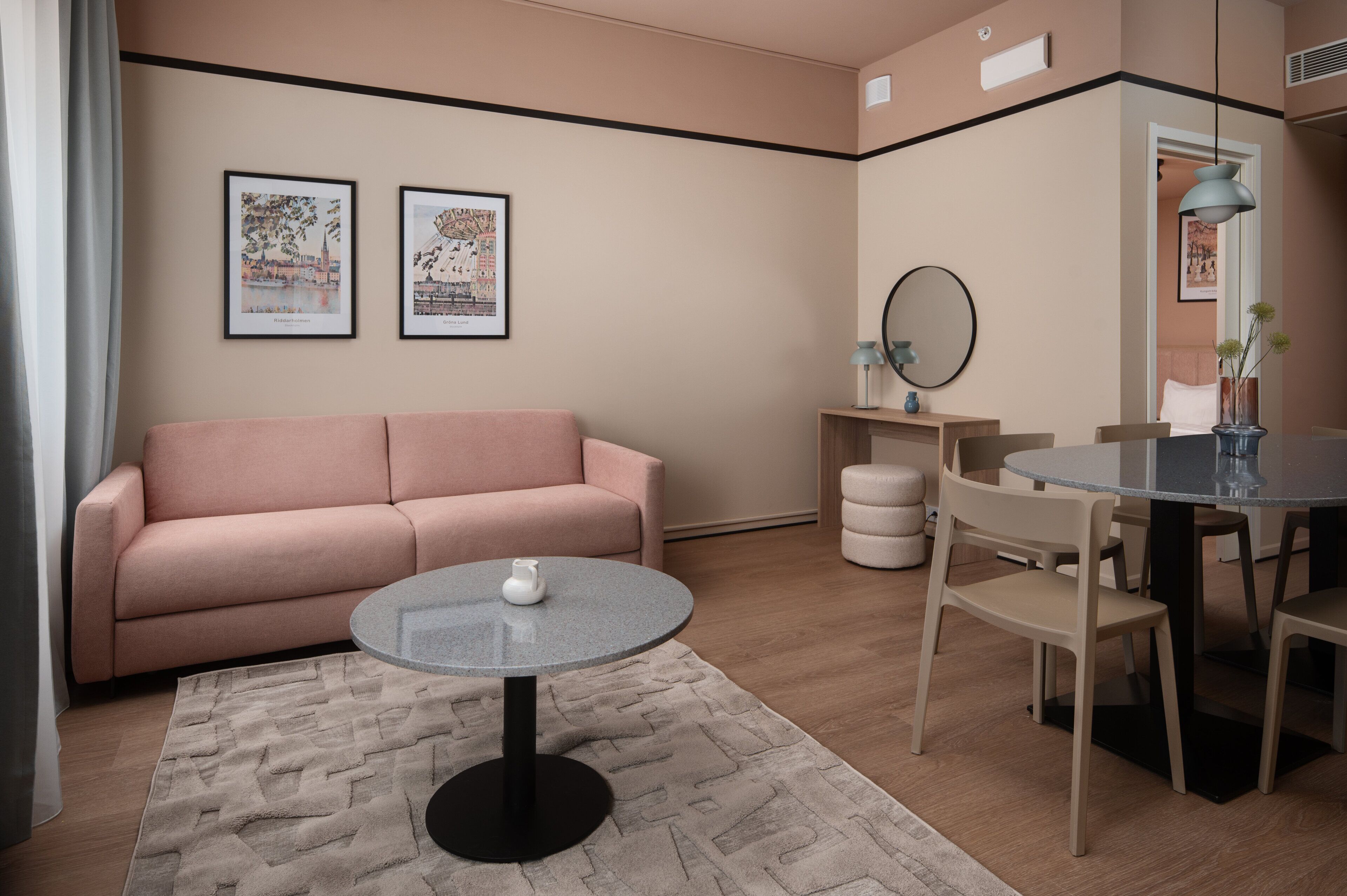 Uma sala de estar moderna com um sofá rosa, uma mesa redonda e uma área de jantar com cadeiras e uma pequena mesa.