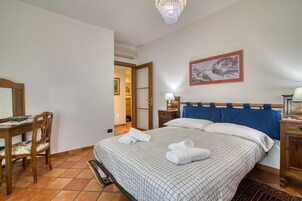 Quarto com cama, escrivaninha, cadeira, mesa de cabeceira, abajur e lustre.