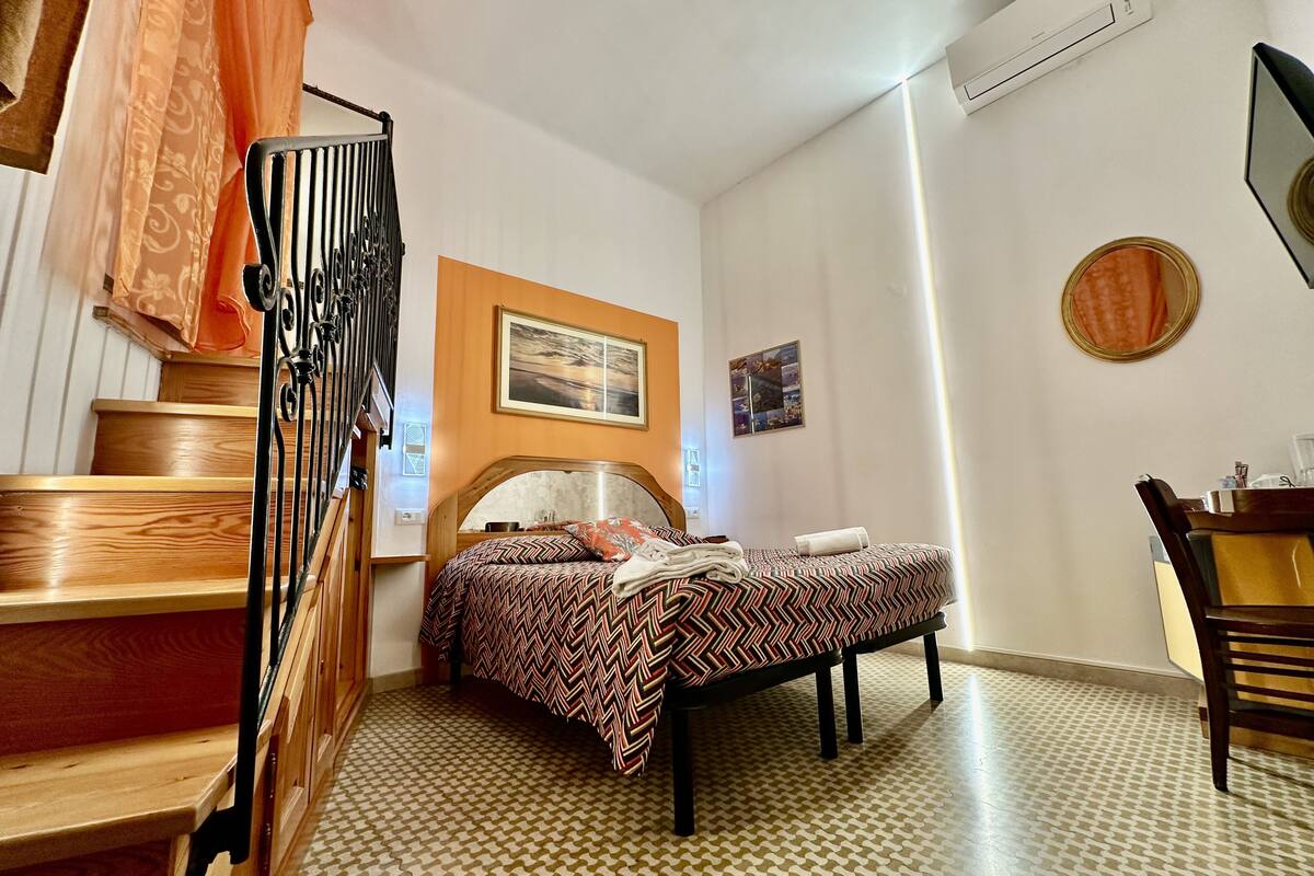 Quarto com cama, escada de madeira, ar condicionado fixado na parede e um quadro emoldurado.