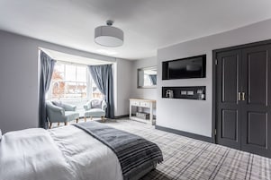 Quarto de hotel moderno com uma cama, duas poltronas, uma escrivaninha, uma televisão e um guarda-roupa.