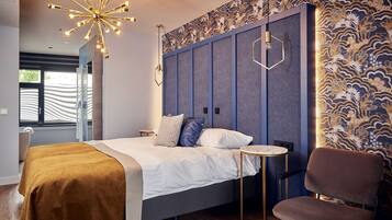 Quarto moderno com uma cama grande, uma mesinha de cabeceira, uma cadeira e um painel decorativo na parede.