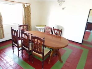 Uma área de refeições com uma mesa de madeira e cadeiras, uma pequena mesa redonda e um tapete de chão verde e vermelho.