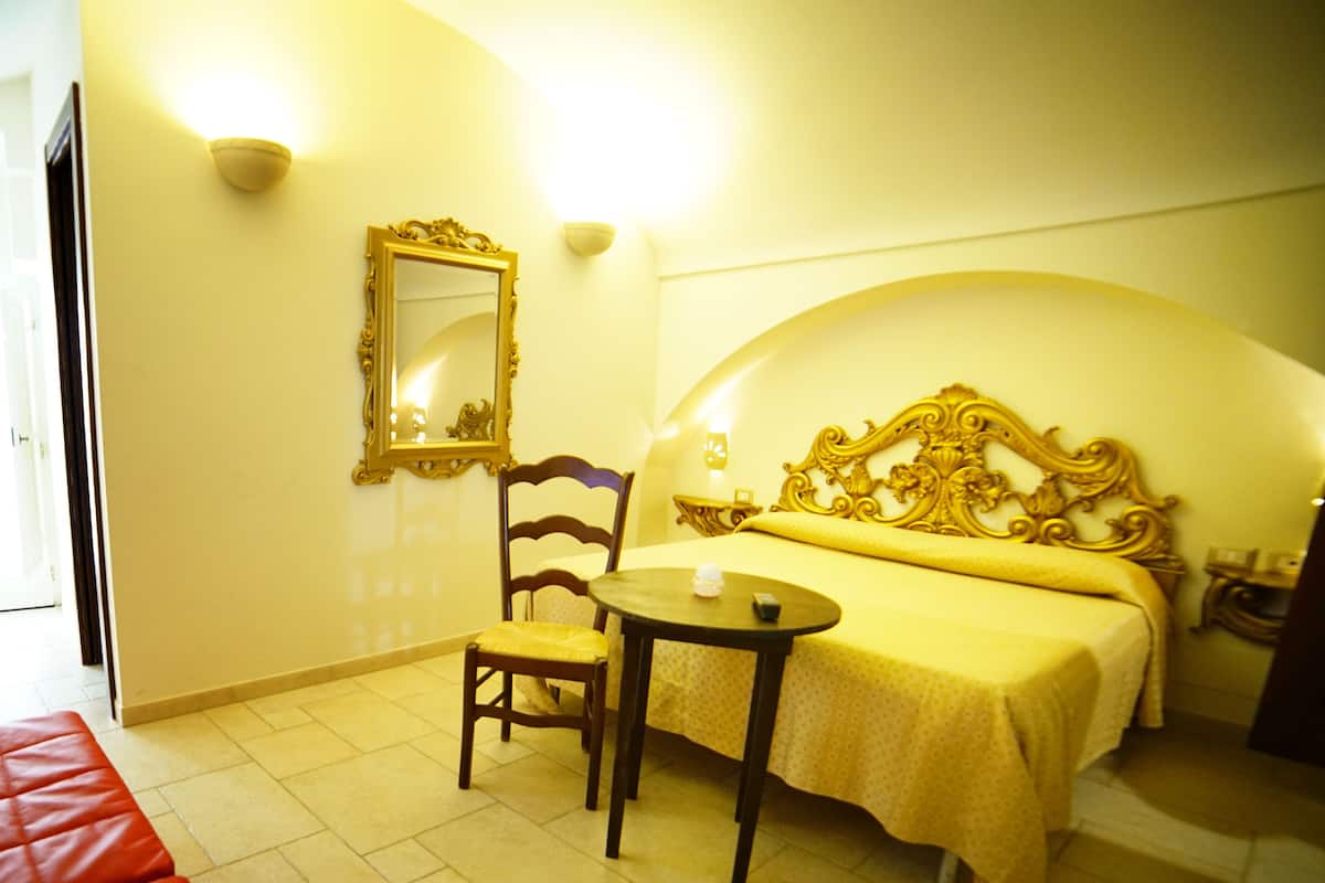 Quarto de hotel com cama, cadeira, mesa pequena, espelho e luminária na parede.