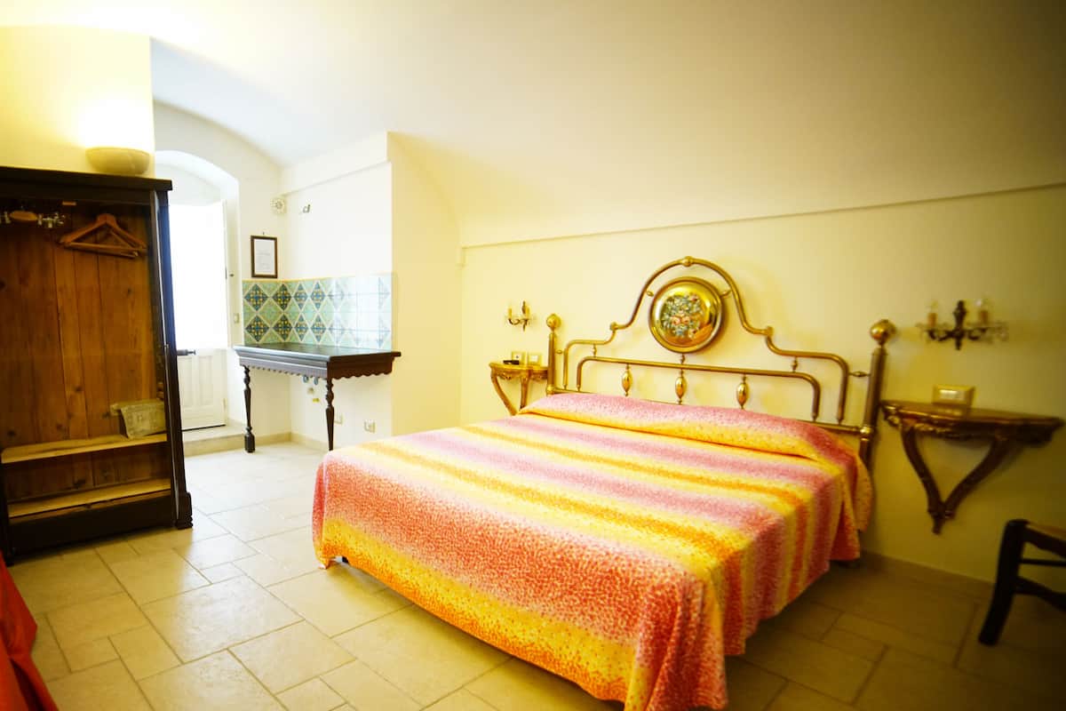 Quarto com cama, guarda-roupa de madeira, mesinha e prateleira na parede.