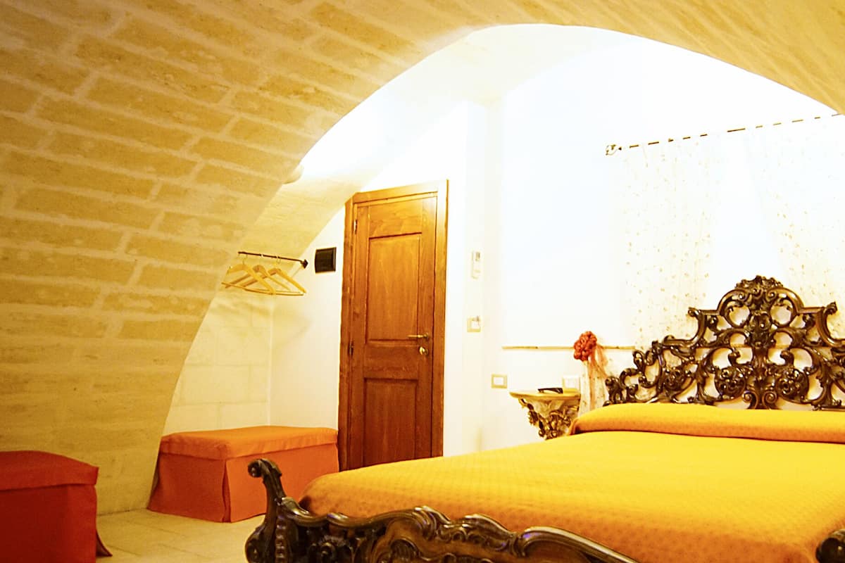 Quarto com cama grande, porta de madeira e parede de tijolos.