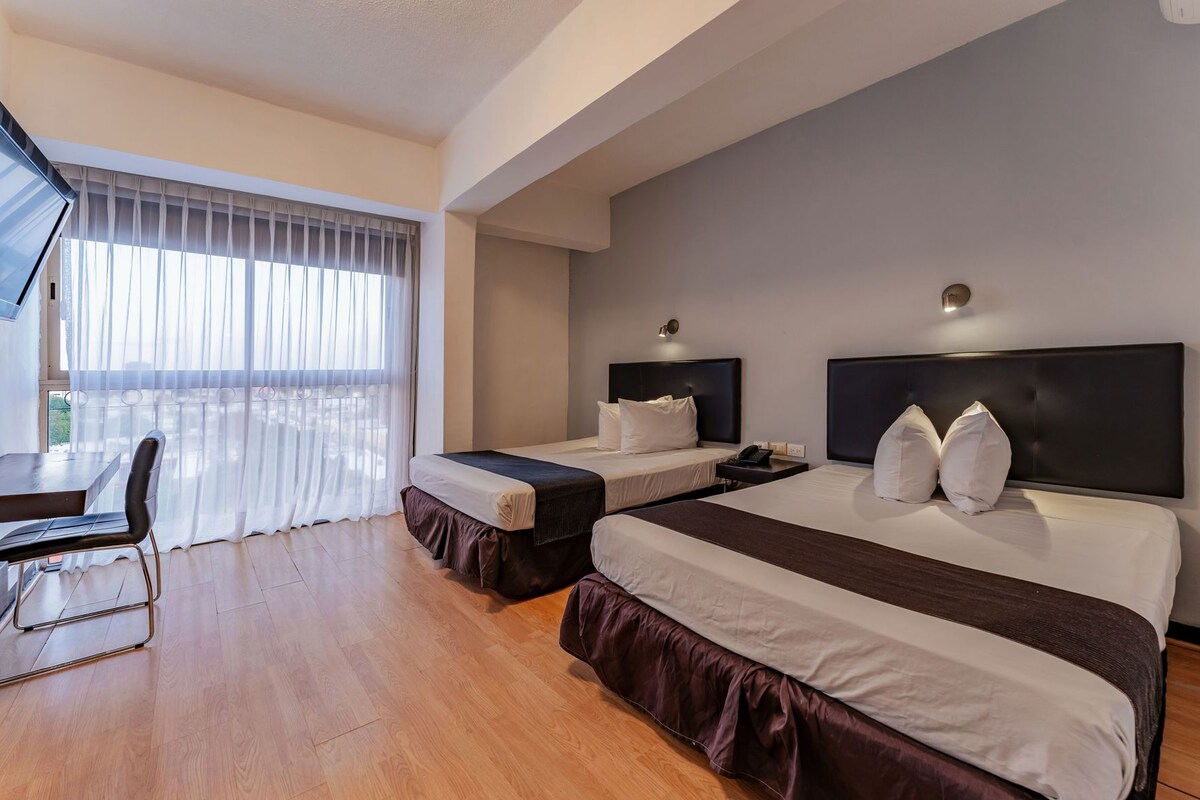 Quarto de hotel com duas camas, uma mesa e uma cadeira.