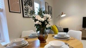 Mesa de jantar posta com pratos, tigelas e talheres brancos, com um vaso de flores brancas no centro.
