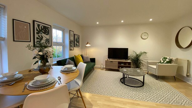 Uma sala de estar moderna com área de jantar, sofá, televisão e um espelho grande.