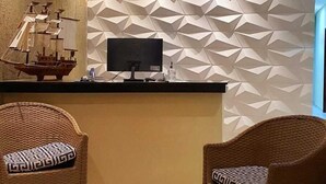 Uma área de recepção com design moderno, apresentando uma parede com padrão geométrico, um modelo de navio e mobiliário de vime.