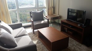 Uma sala de estar moderna com sofá, poltrona, mesa de centro, TV e escrivaninha de vidro.