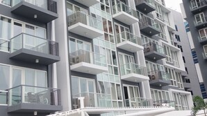 Um edifício moderno de arranha-céu com várias varandas, grandes janelas e uma área externa coberta com assentos.