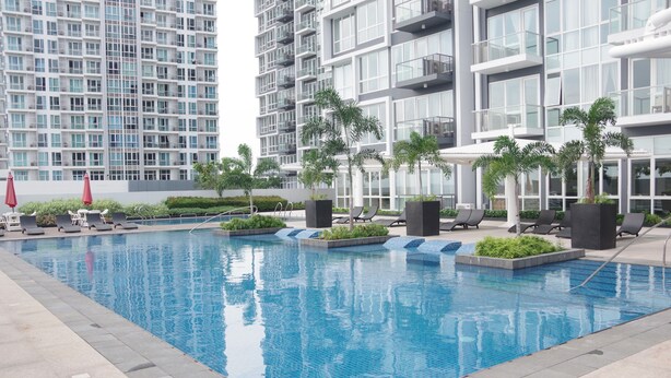 Uma área de piscina moderna em hotel, com uma piscina retangular, espreguiçadeiras e plantas em vasos.
