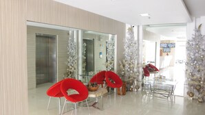 Um lobby moderno com elevador de vidro, cadeiras vermelhas, uma mesa de vidro e decorações de Natal.