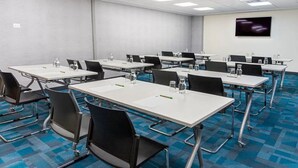 Uma sala de conferências com mesas, cadeiras e uma tela de televisão.
