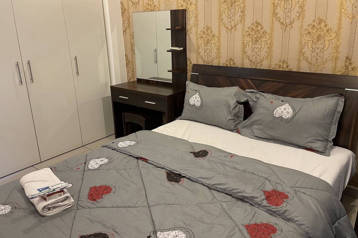Um quarto com uma cama, penteadeira, espelho e guarda-roupa.