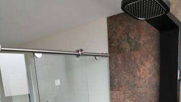 Casa de banho moderna com cabine de duche em vidro, sanita branca e suporte de toalhas preto.