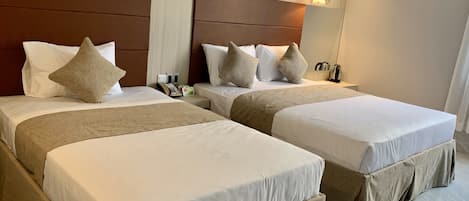 Quarto de hotel com duas camas, cada uma com lençóis brancos e cabeceiras bege. Há um telefone e uma cafeteira na mesinha de cabeceira.