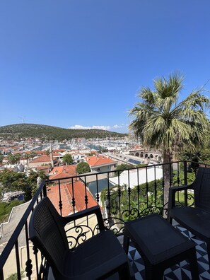 Uma varanda com vista para um porto, palmeiras e edifícios com telhados vermelhos.