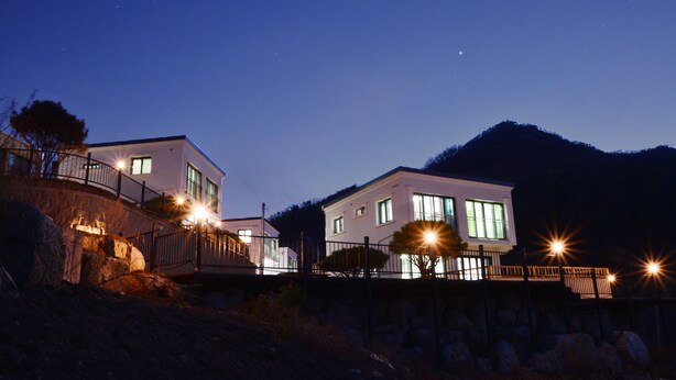 Uma casa de dois andares com um muro de pedra e uma montanha ao fundo.