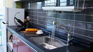 Uma cozinha moderna com pia de aço inoxidável, uma garrafa de vinho, um rolo de massa e uma xícara sobre o balcão.