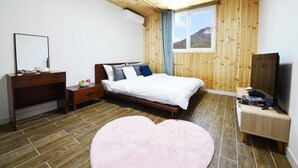 Quarto com cama de madeira, mesa de cabeceira, cômoda, espelho e janela com vista para uma montanha.
