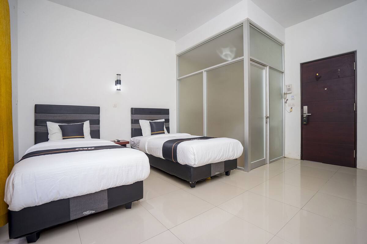 Quarto de hotel com duas camas, uma porta de vidro deslizante e uma porta de madeira escura.