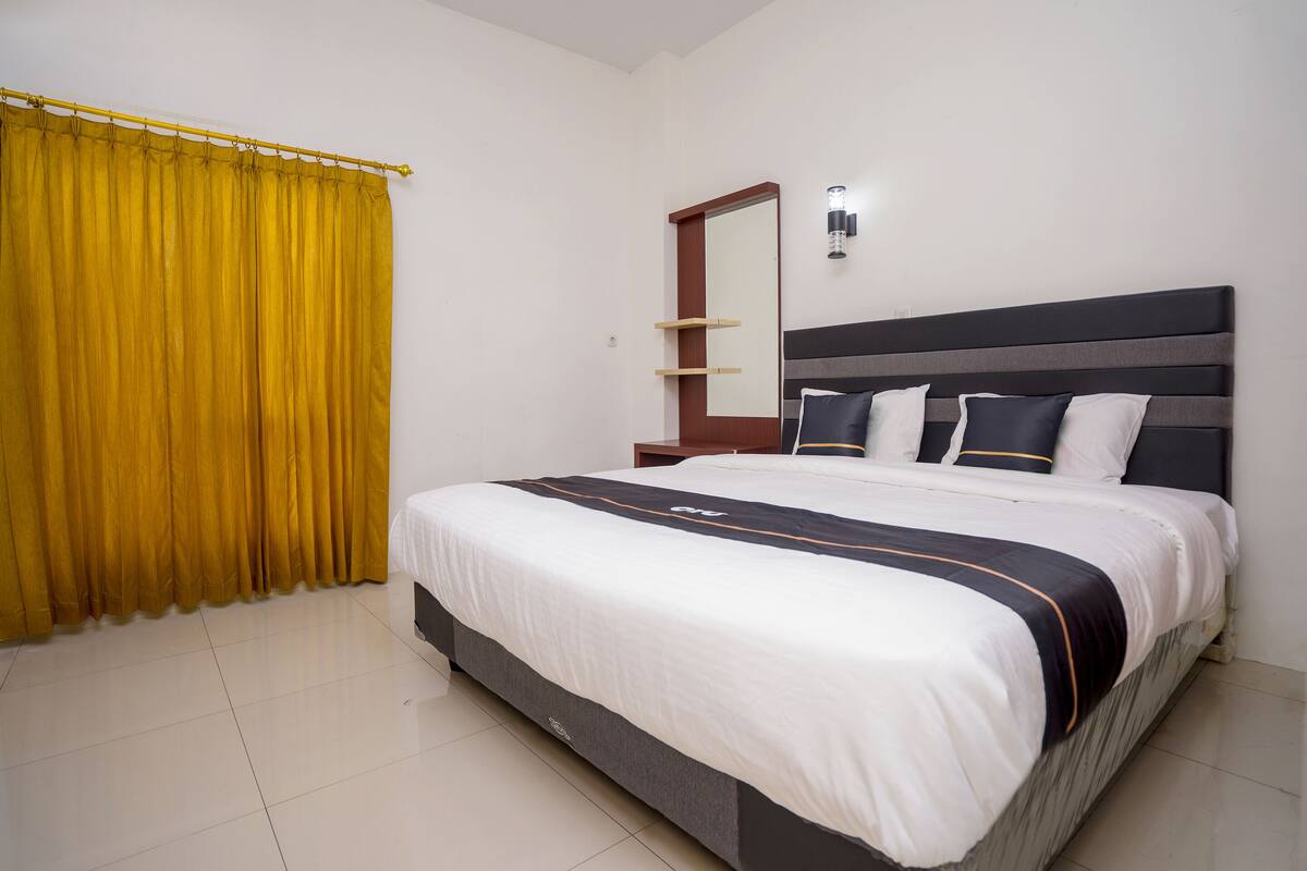 Quarto bem arrumado com uma cama, um espelho e uma cortina amarela.