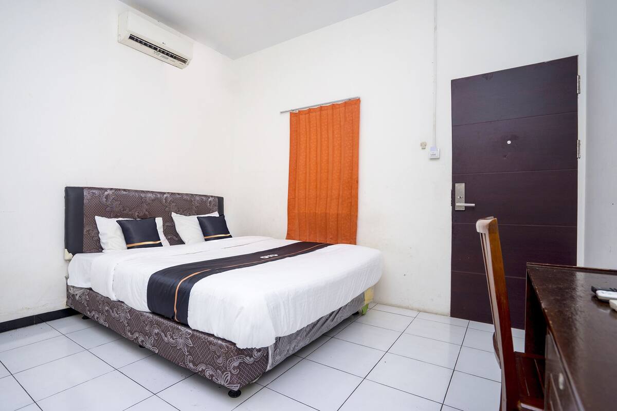 Uma cama bem arrumada com cabeceira estampada, cortina laranja e porta escura.