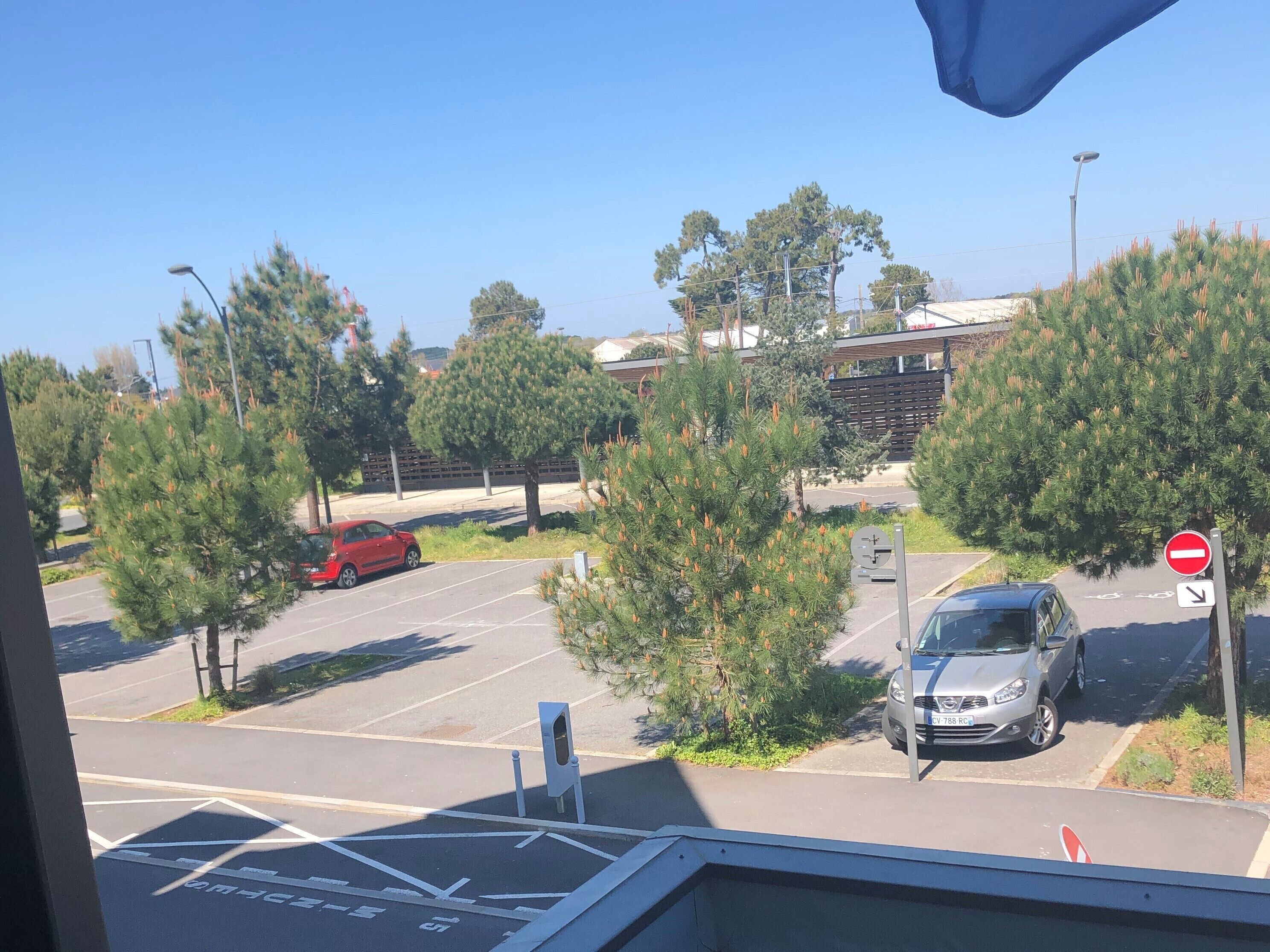 Um parque de estacionamento com carros, árvores e um sinal de proibido estacionar.
