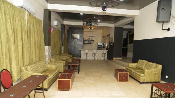 Um saguão de hotel com sofás, mesas, área de bar e uma televisão.