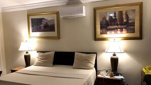 Quarto de hotel com uma cama, duas luminárias de cabeceira, uma escrivaninha com cadeira e dois quadros na parede.
