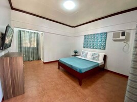 Quarto com cama, televisão, janela com cortinas e ar condicionado fixado na parede.