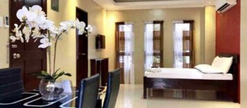 Quarto de hotel com cama, mesa de jantar e cadeiras, e um vaso de flores.