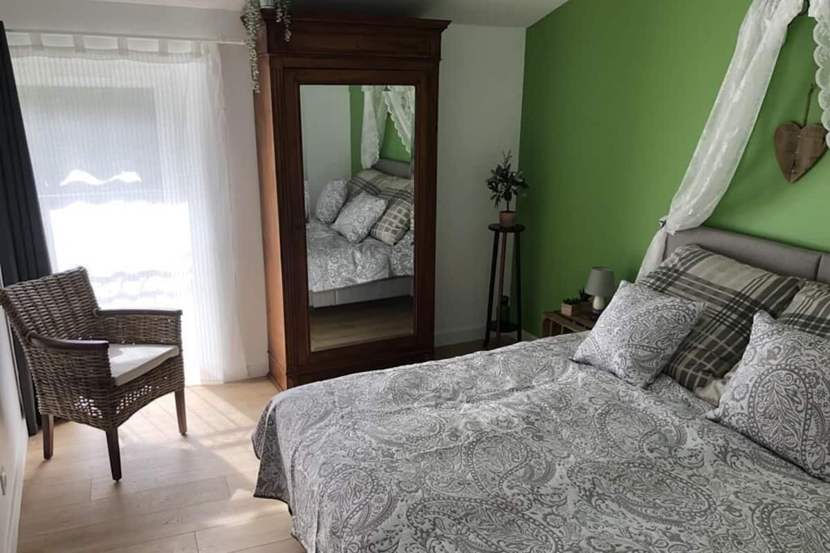 Quarto com cama, uma cadeira, um espelho e parede verde.