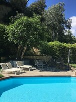 Piscina com espreguiçadeiras e um muro de pedra ao fundo.