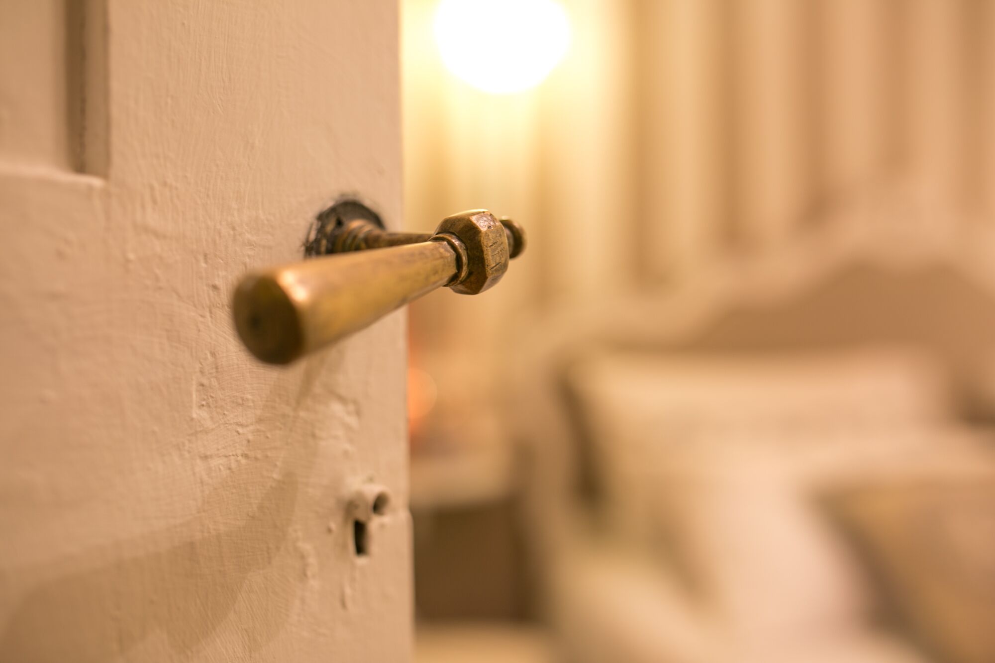 Um close-up de uma maçaneta de latão em uma porta branca, com um olho de fechadura, emoldurado por um fundo suavemente iluminado.