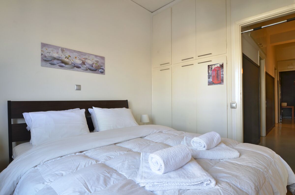 Uma cama bem arrumada com lençóis brancos e toalhas dobradas, um quadro na parede e um guarda-roupa com porta.