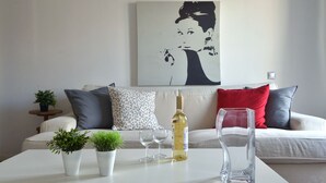 Uma sala de estar com um sofá branco, uma mesa de centro com plantas, uma garrafa de vinho e um vaso de vidro.