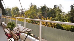 Uma varanda com mesa e cadeiras, um vaso de planta e vista para árvores e folhagem.
