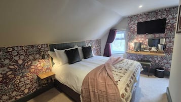 Um quarto com cama, mesa de cabeceira, televisão e janela.