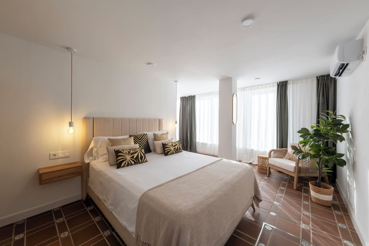 Quarto de hotel moderno com uma cama grande, mesa de cabeceira e um vaso com planta.